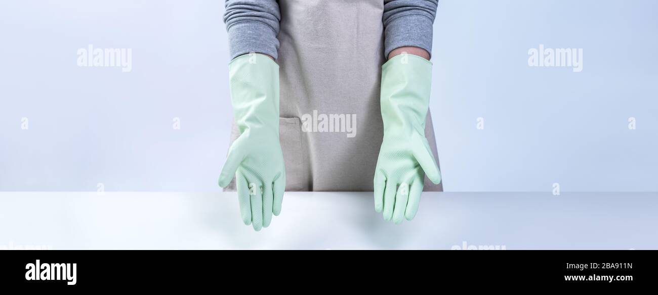 Young woman housekeeper in apron is wearing green gloves to clean the ...