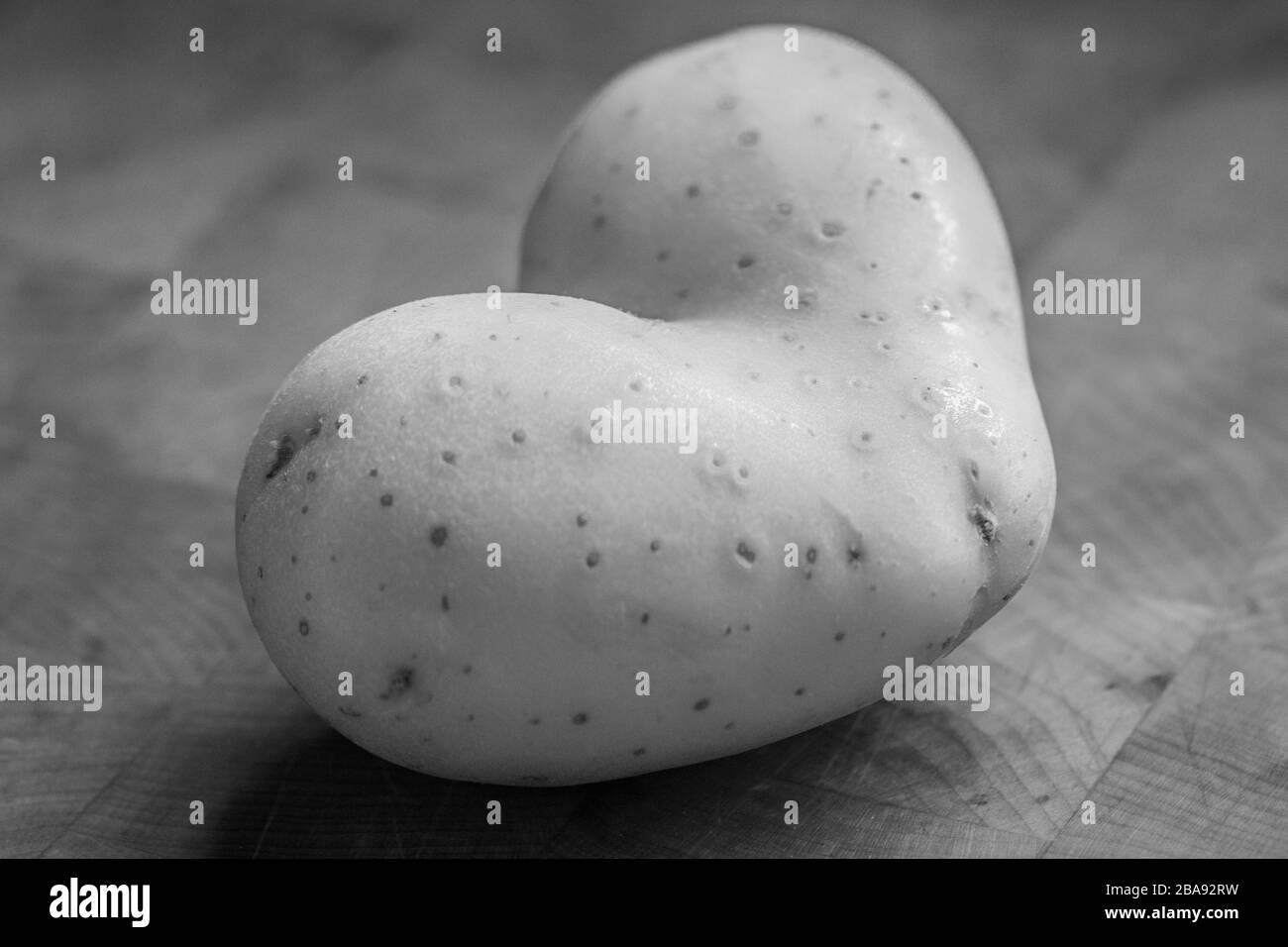 Isolated close up of a single heart shaped raw potato in black and ...