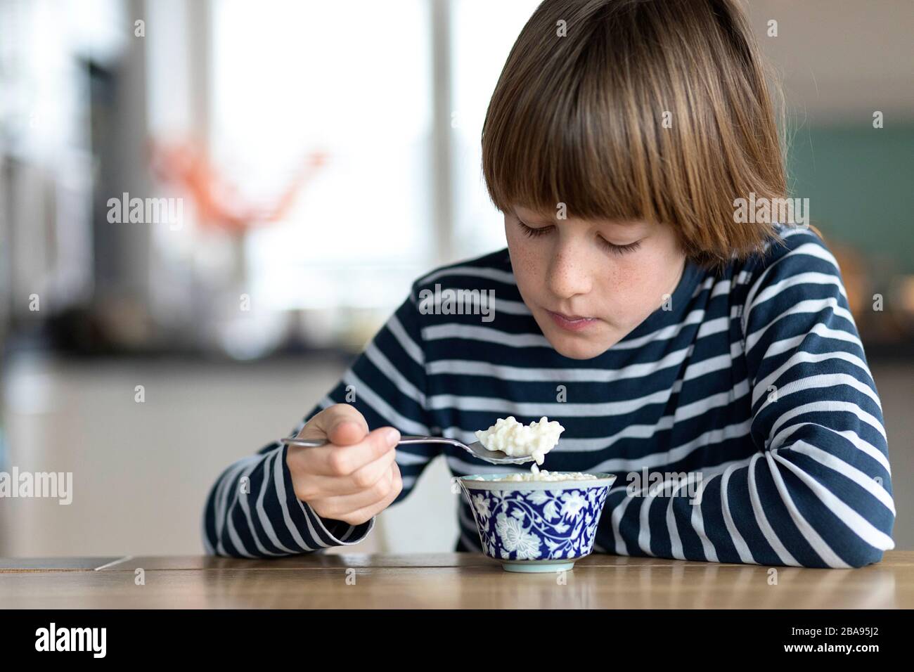 Child eating rice pudding at the kitchen table Stock Photo - Alamy