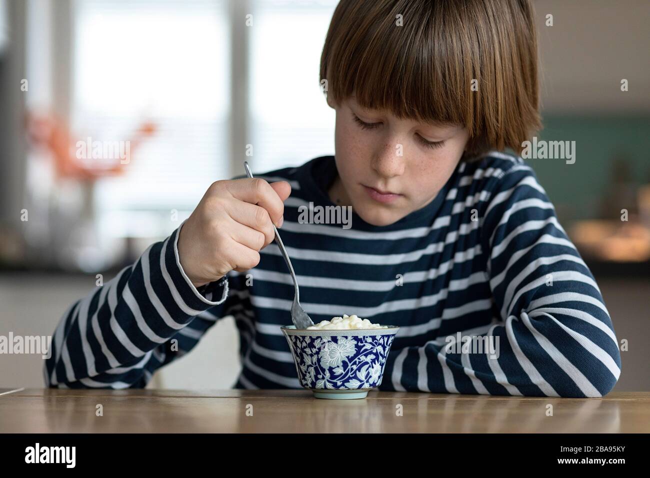 Child eating rice pudding at the kitchen table Stock Photo - Alamy