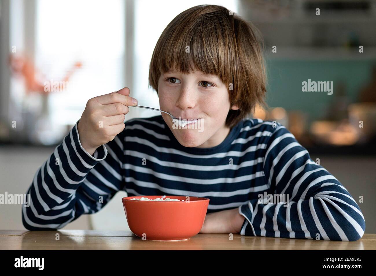 Child eating rice pudding at the kitchen table Stock Photo - Alamy