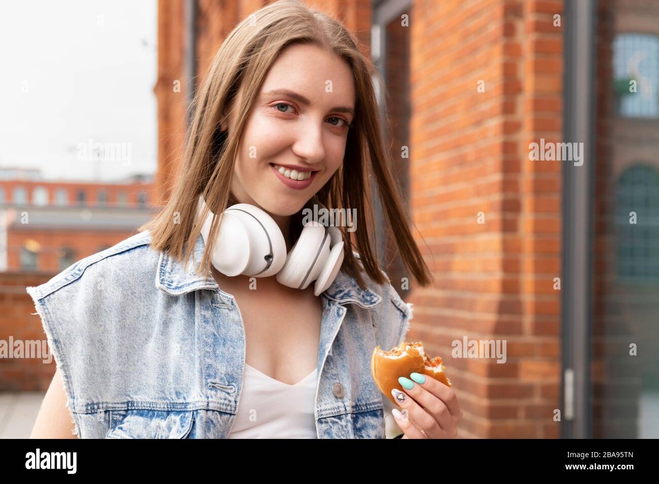 A young girl is eating her burger right on the street. She has fun ...
