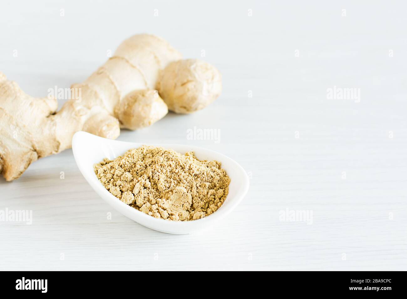 Fresh ginger root and ground ginger spice on white wooden table ...