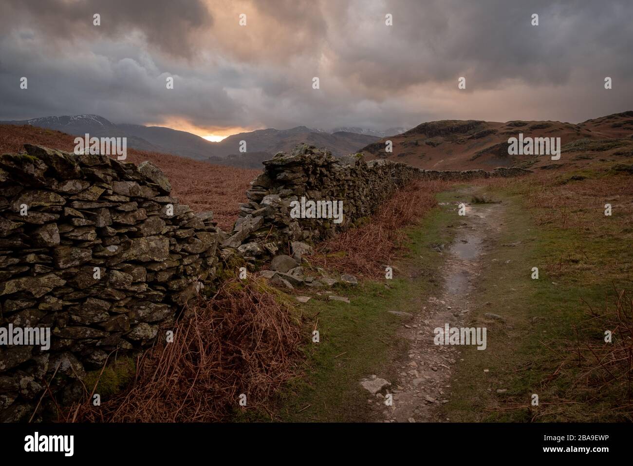 Sunset over Wrynose Pass seen from behind a dry stone wall on Loughrigg ...