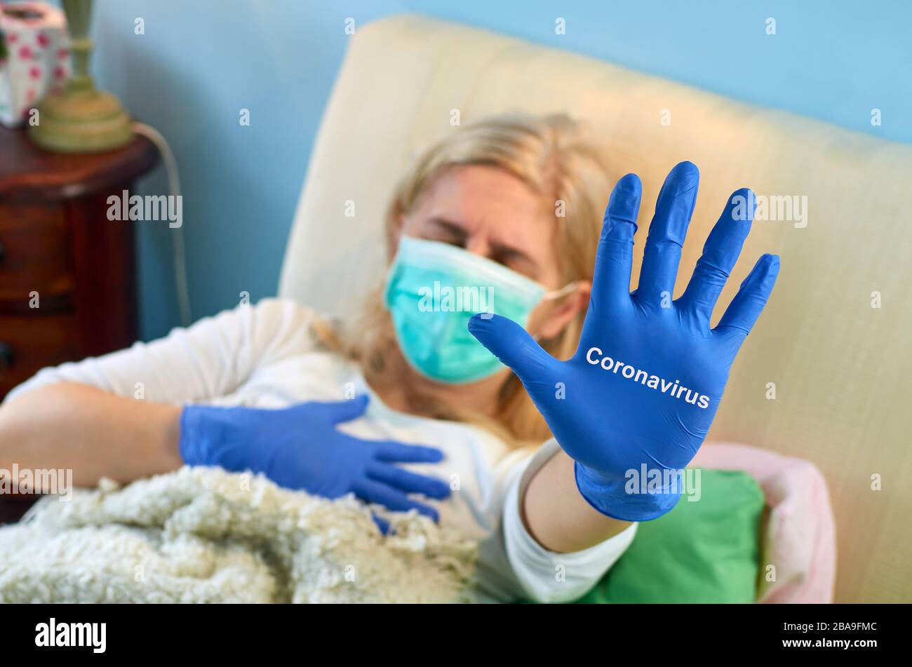 Woman lying sick in a bed with a raised hand showing to keep a distance ...