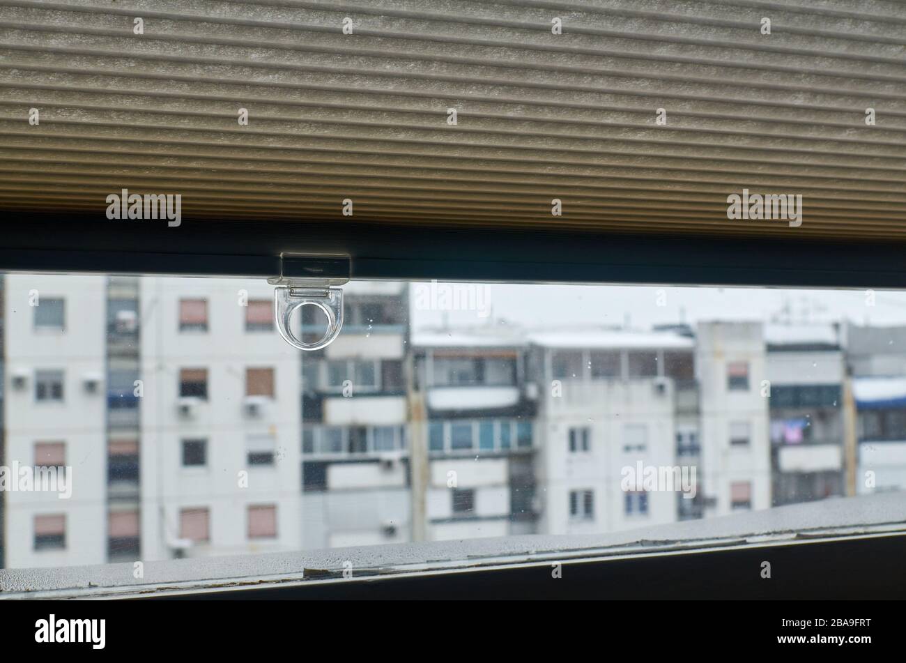 View through a window with a half raised blind to a next residential ...
