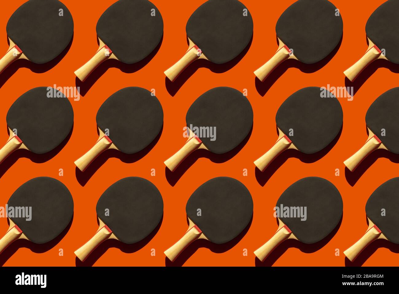 Repeating black tennis ping pong rackets with a hard shadow on a orange ...