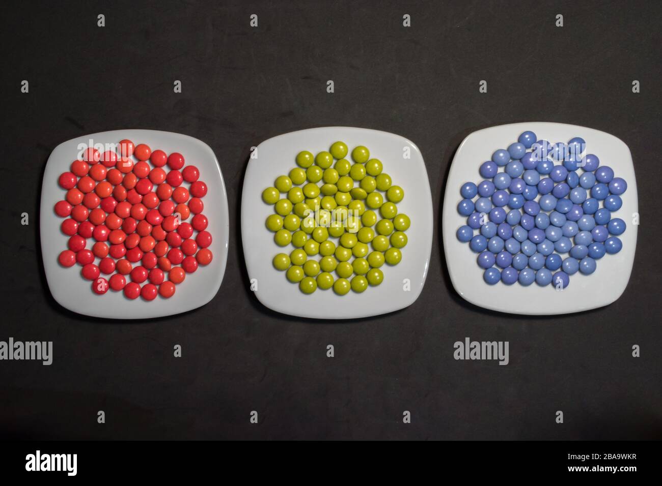 Three plates with colorful candies of chocolates with RGB colors on ...