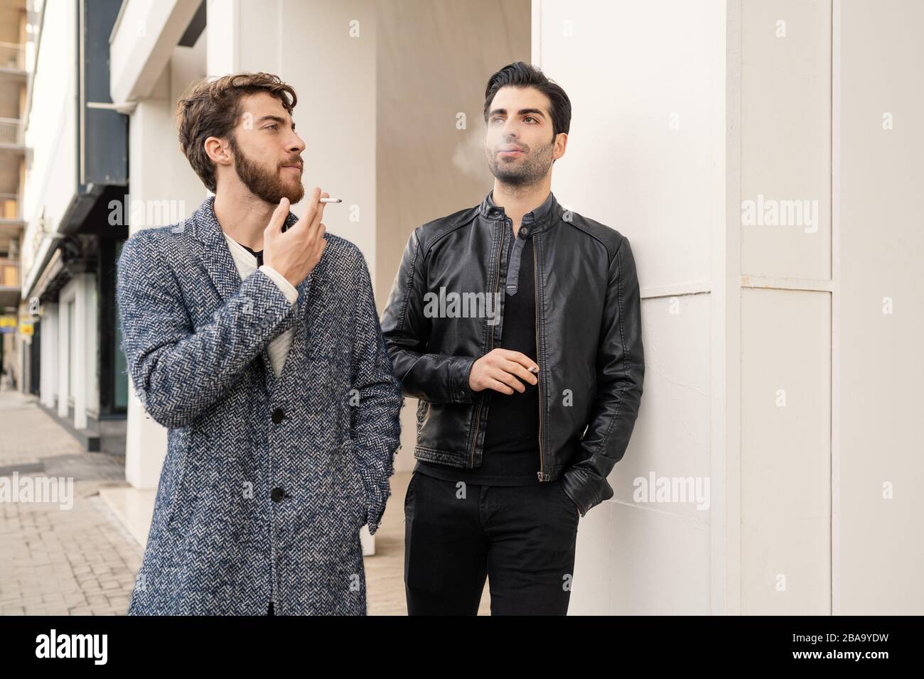 Young elegant people talking and smoking together outdoors in the city ...