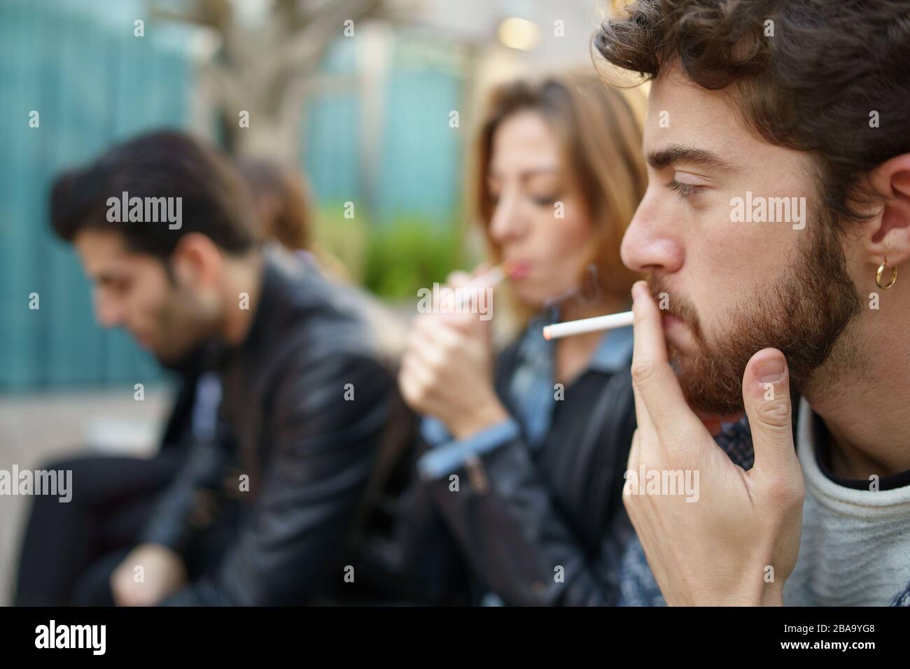Young people smoking outdoors sitting on a bench. Youth addiction ...
