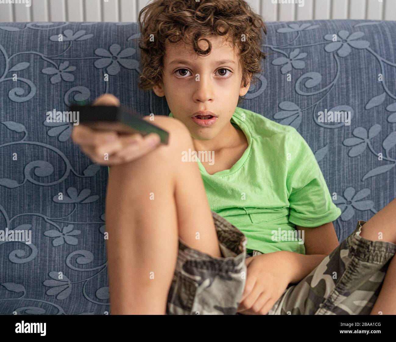 Kid on the sofa watching TV and changing channels with a TV remote ...