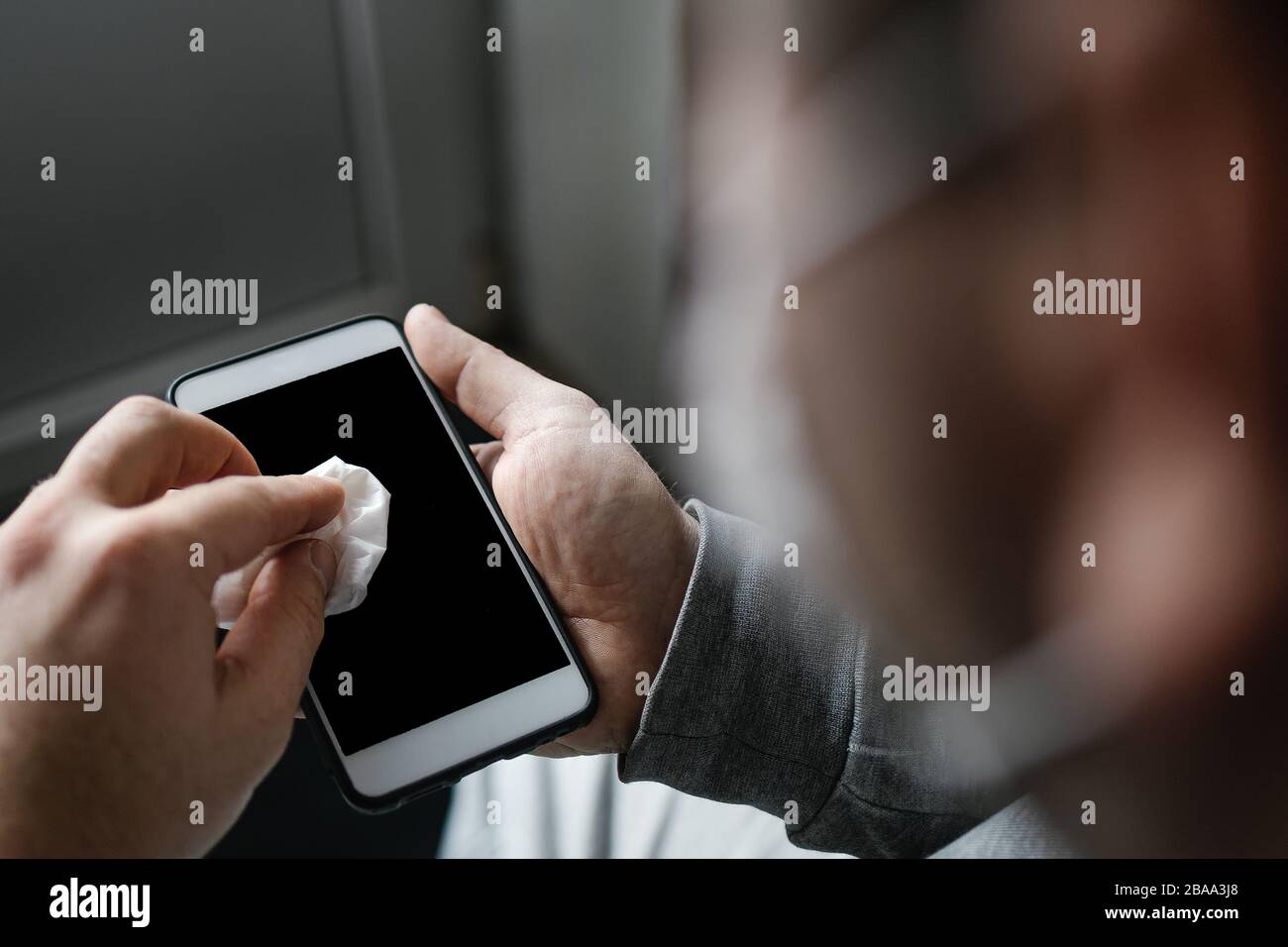 Masked man cleaning smartphone screen with alcohol or disinfectant. The ...