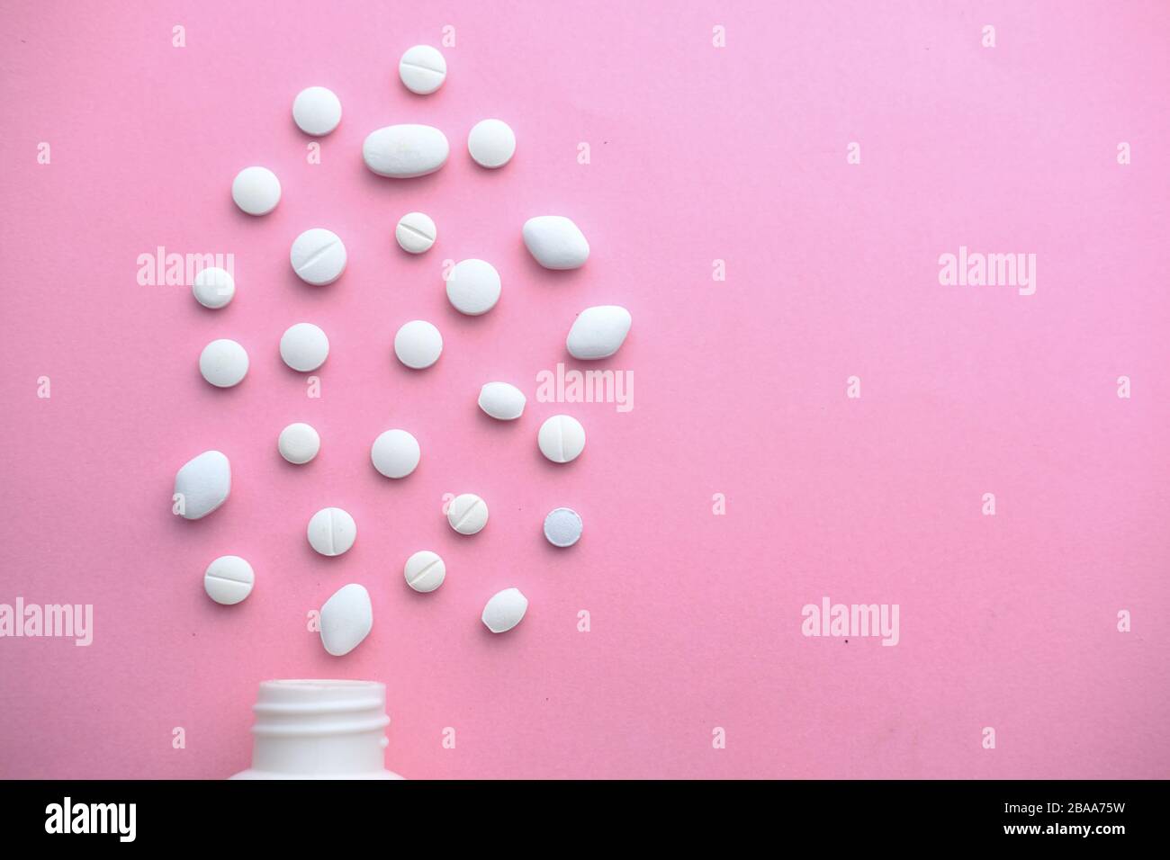 white color pills spilling from container on pink background, close up ...