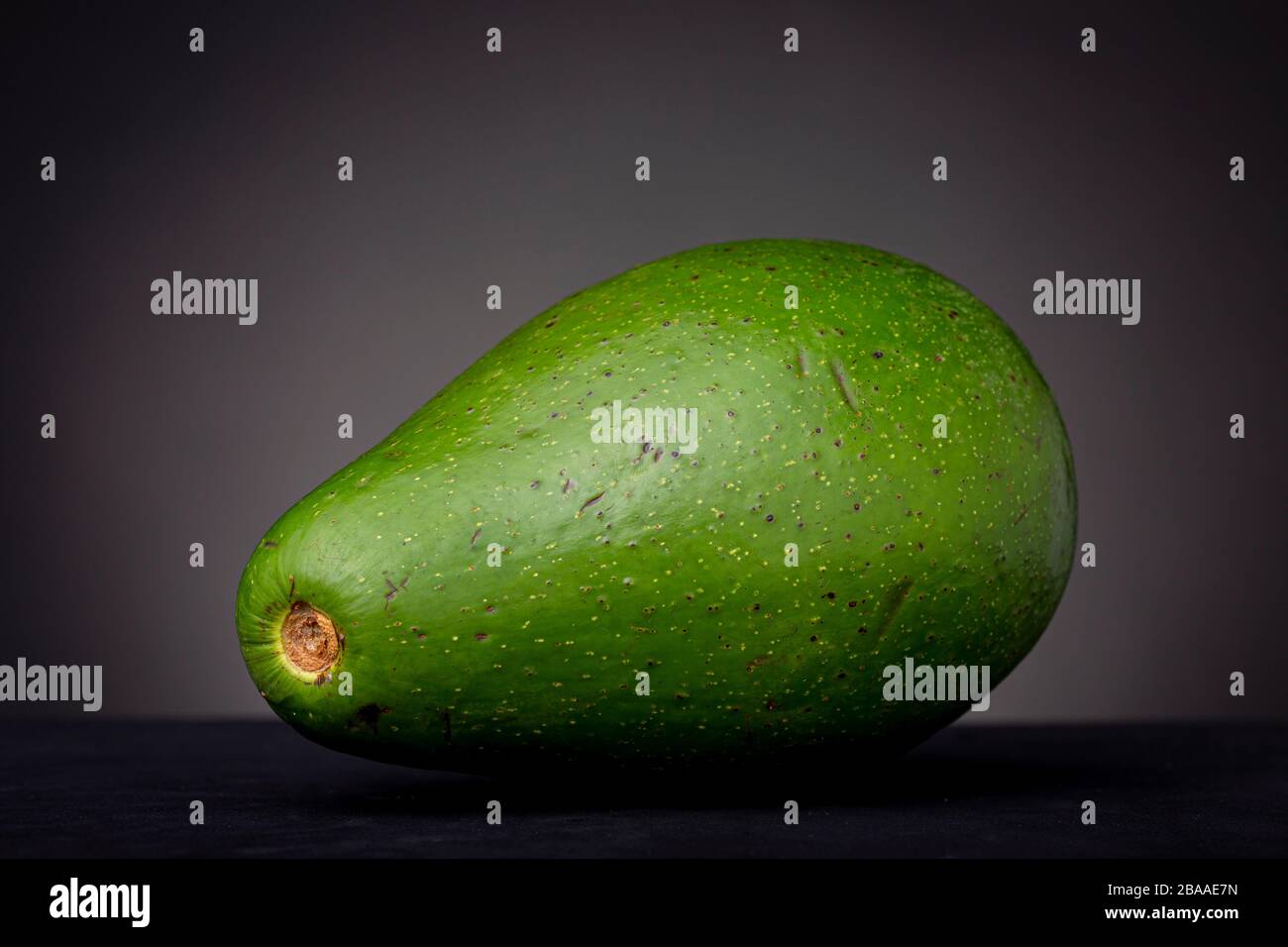 Large pear-shaped vibrant green avocado laying on a black surface ...