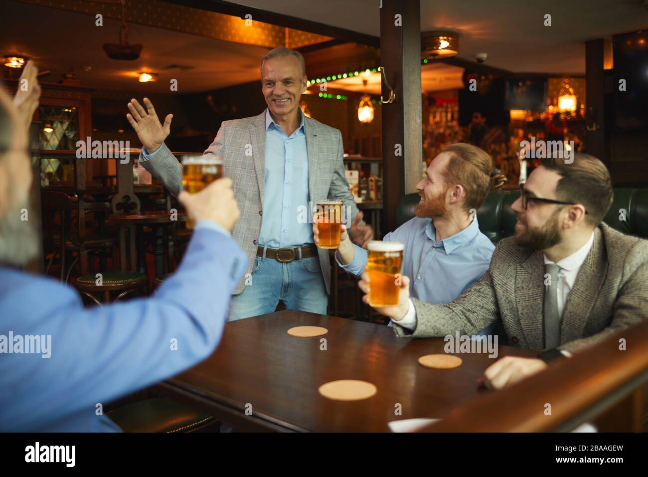 Group of businessmen greeting their colleague while sitting in cafe and ...