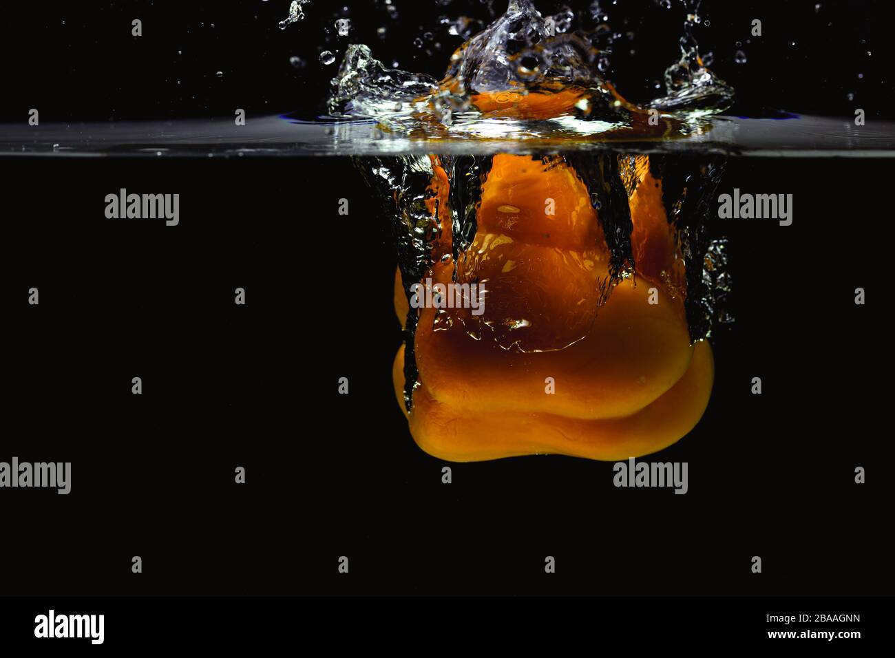 Close up view of colorful yellow pepper falling in water on black ...