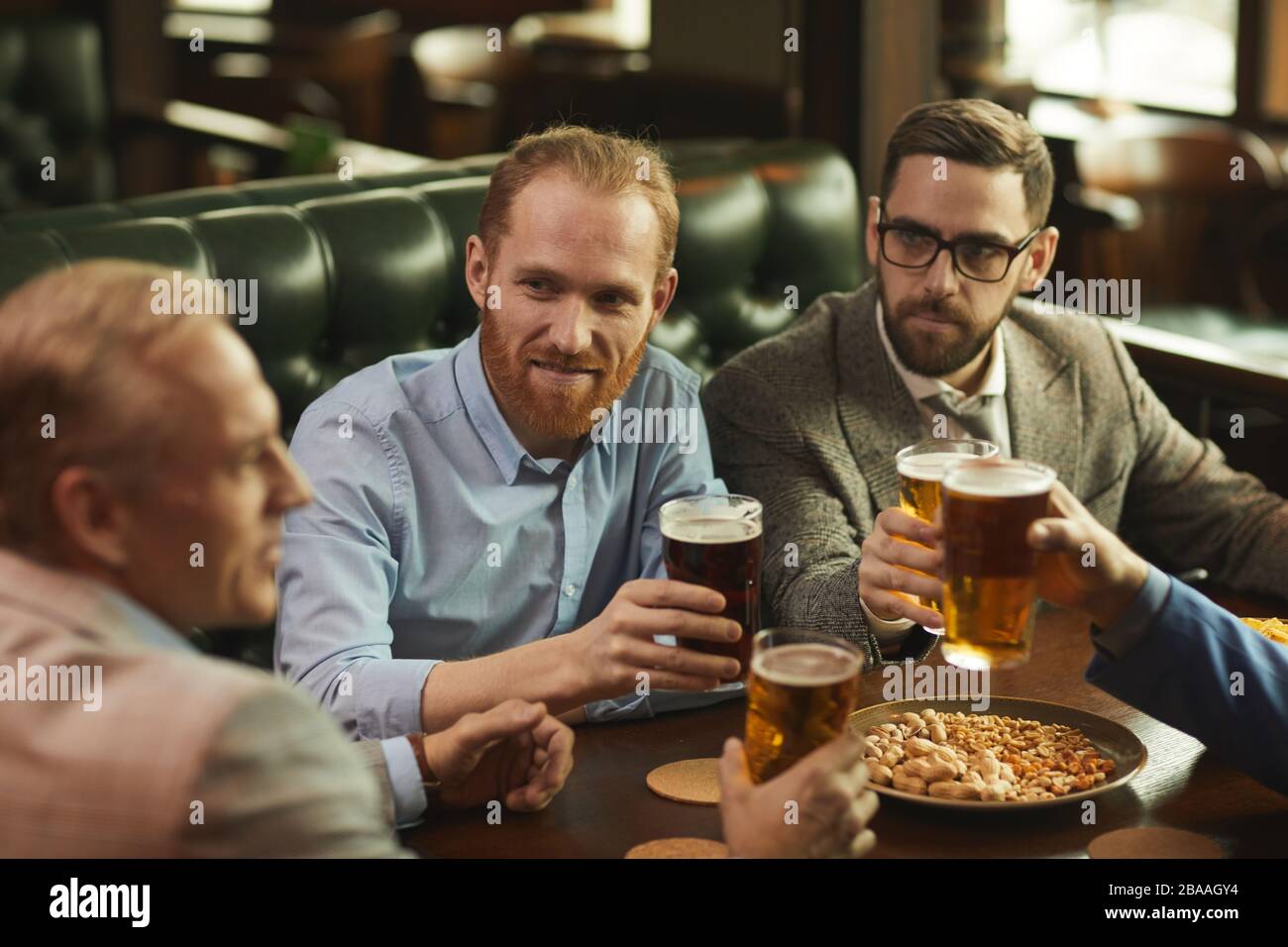 Group of colleagues sitting at the table drinking beer with peanuts and ...