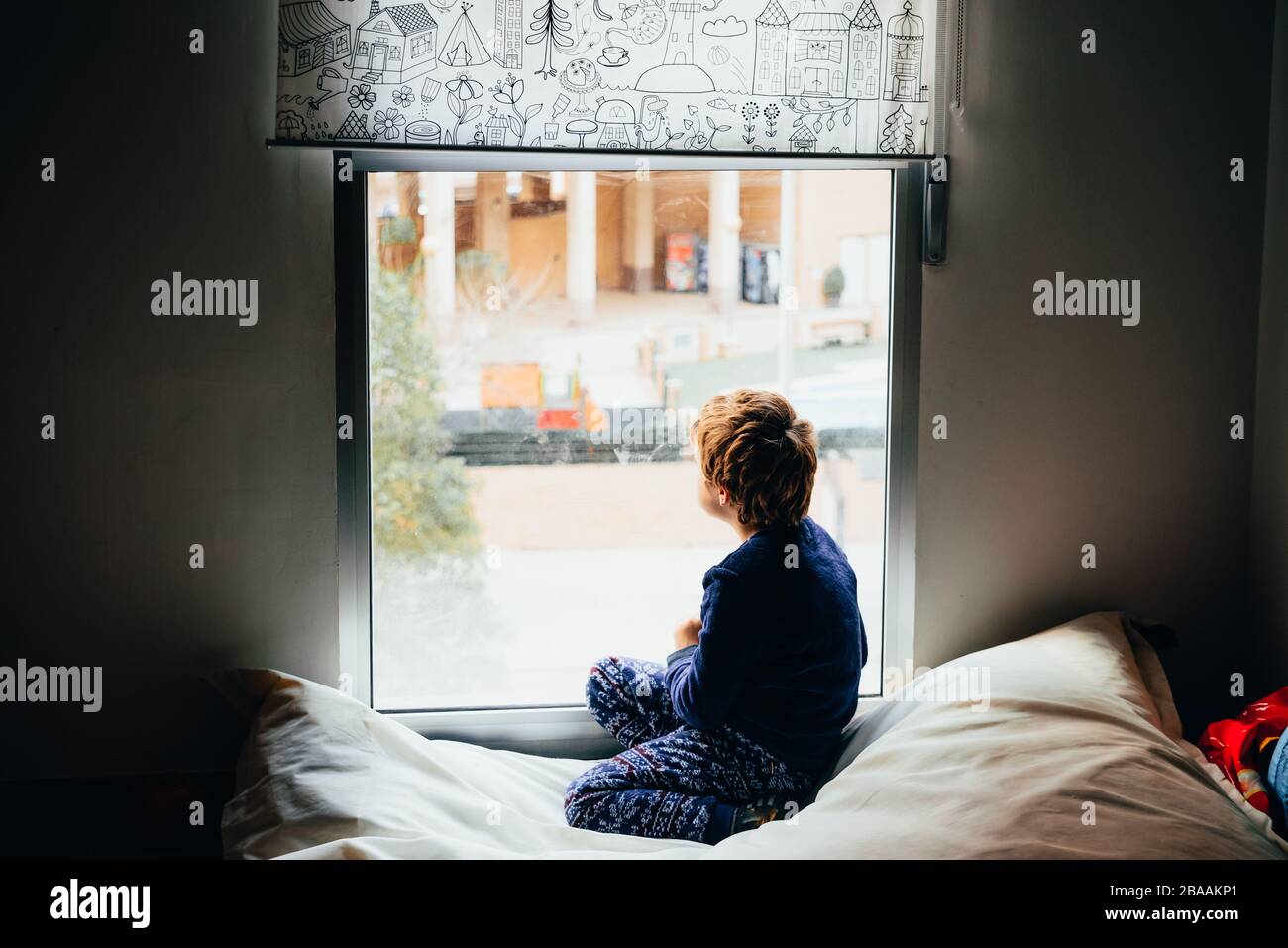 Sad and melancholic boy looks through a window in his apartment during ...