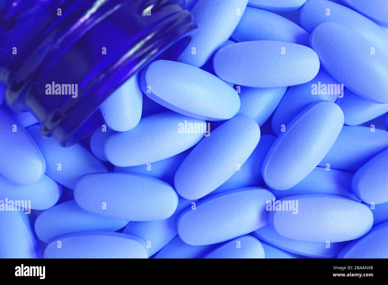 Top view of blue oval shaped pills scattered from vivid blue glass ...