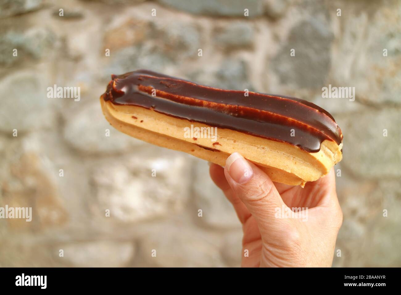 Hand Holding a Chocolate Eclair with Blurry Stone Wall in Background ...