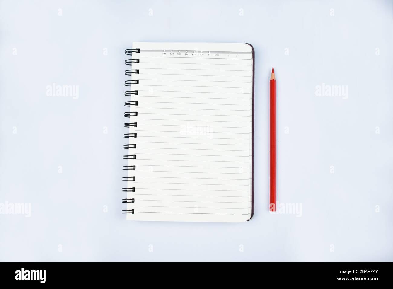 A red wood pencil crayon beside a white notebook before an isolated ...