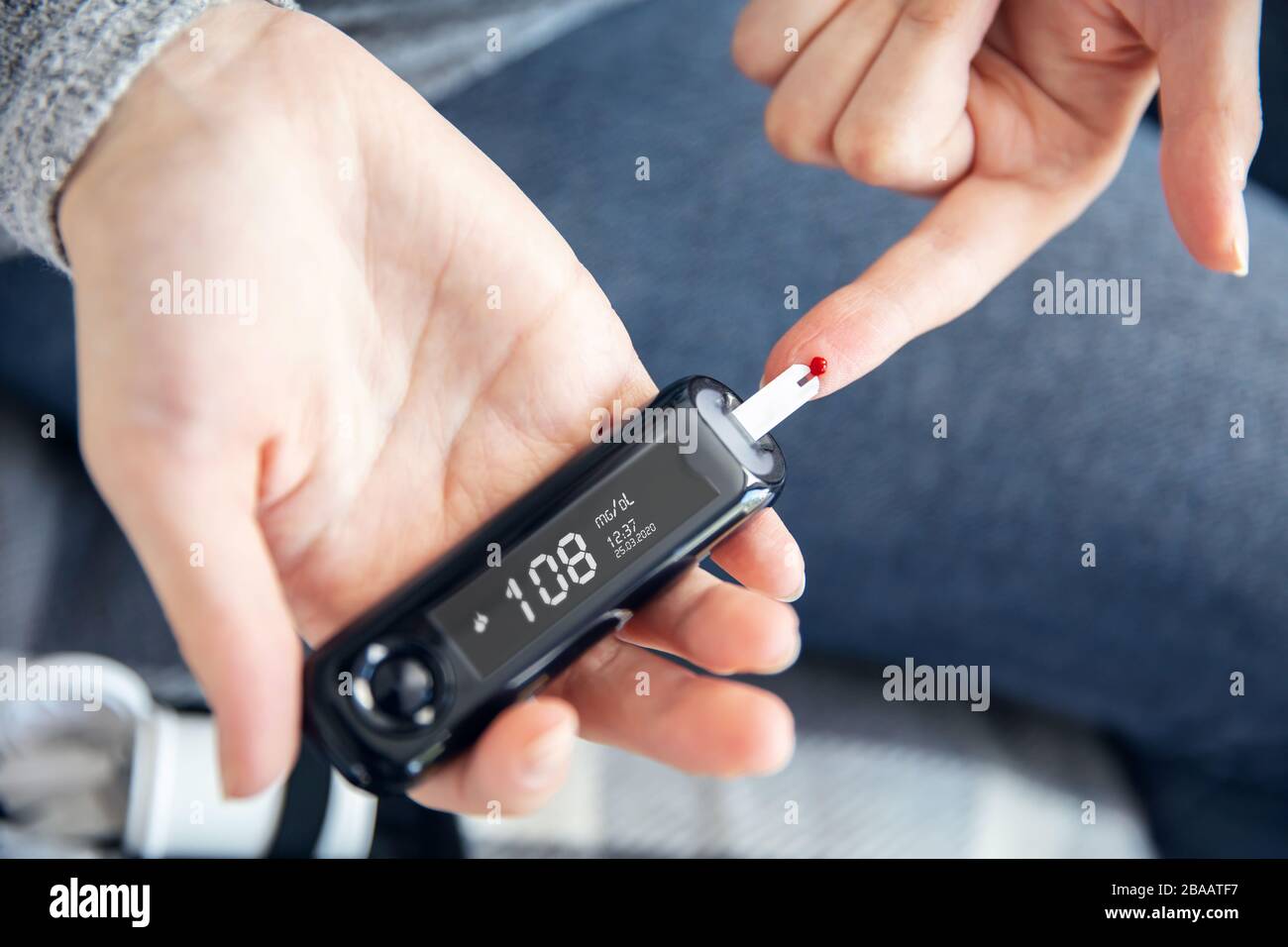 Woman checks her blood glucose level with modern glucometer at home ...