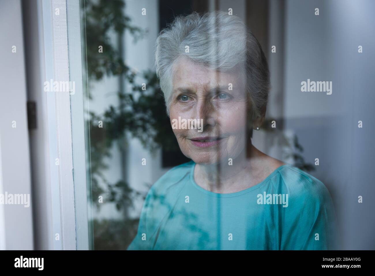 Caucasian senior woman looking over the window at home Stock Photo - Alamy