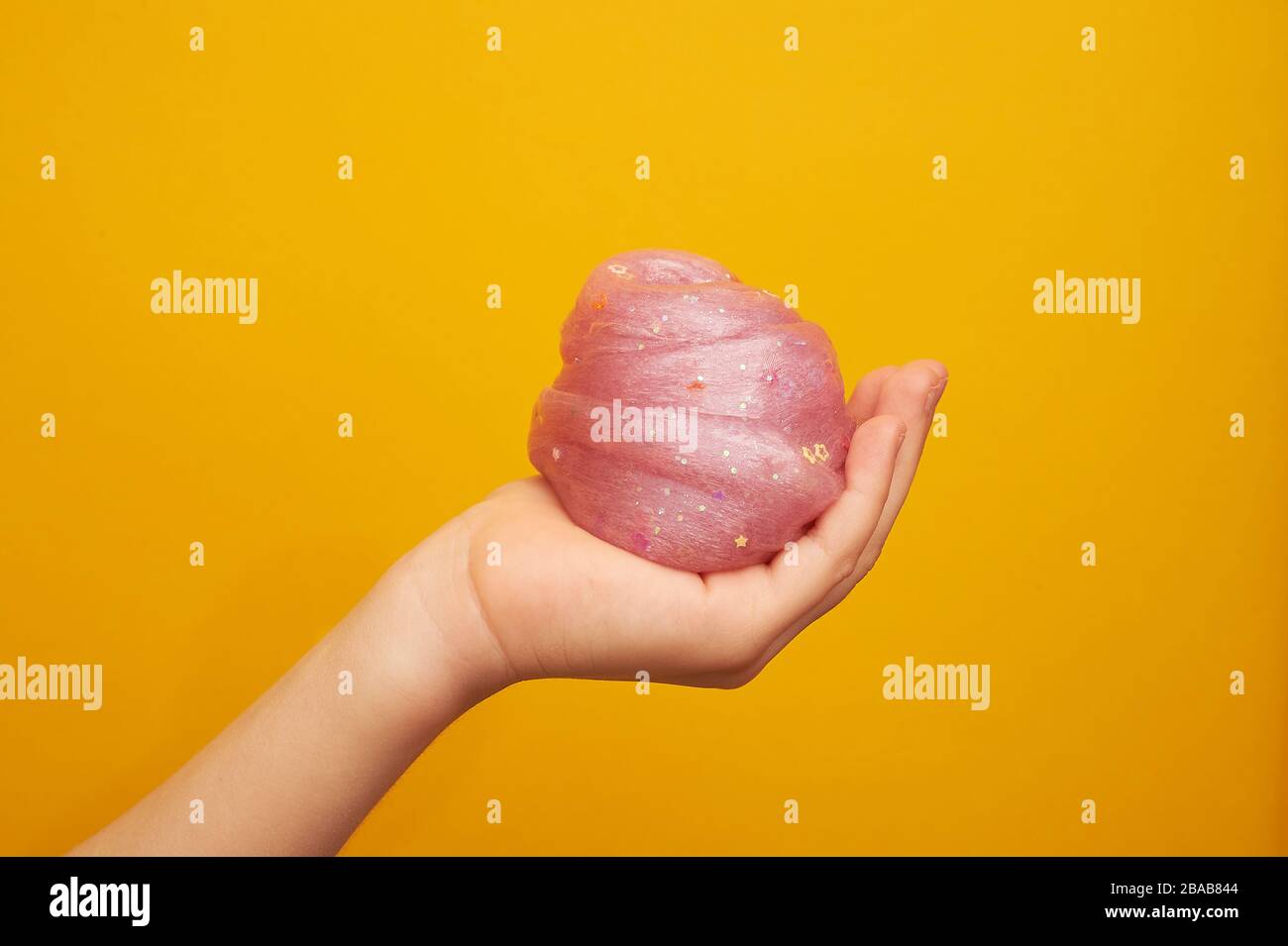 Pink slime with sequins, in a child's hand, on a yellow background ...
