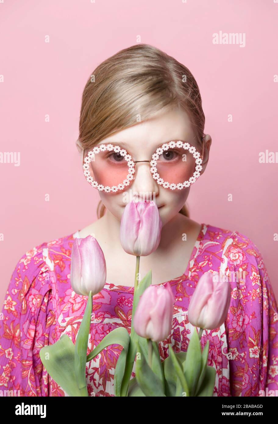 Mod tween girl smelling pink tulips against pink backdrop, portrait ...