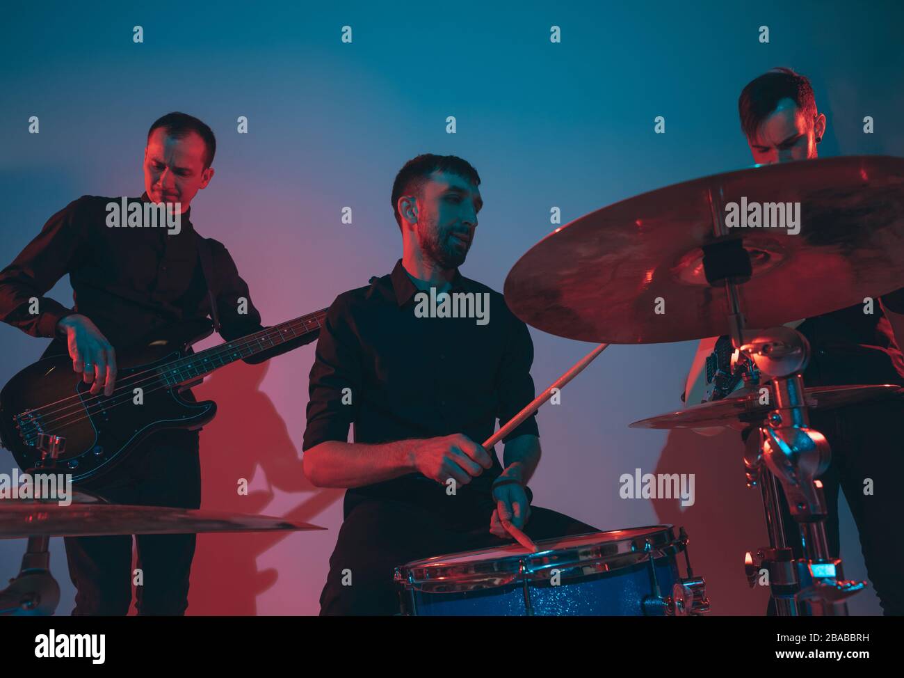 Young caucasian musicians, band performing on blue studio background in ...