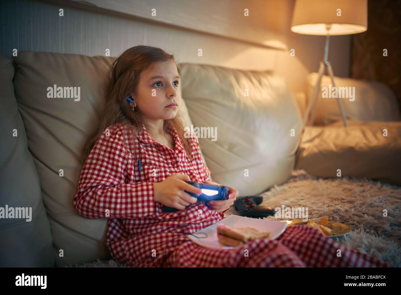 Happy little girl in pajams sitting on sofa, eating pizza and playing ...