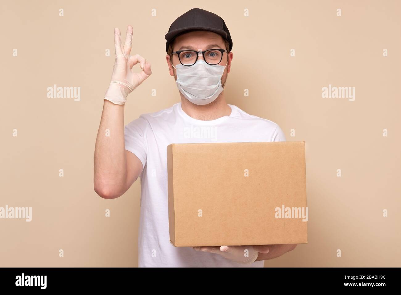 Smiling young delivery man holding and carrying a cardbox showing ok ...