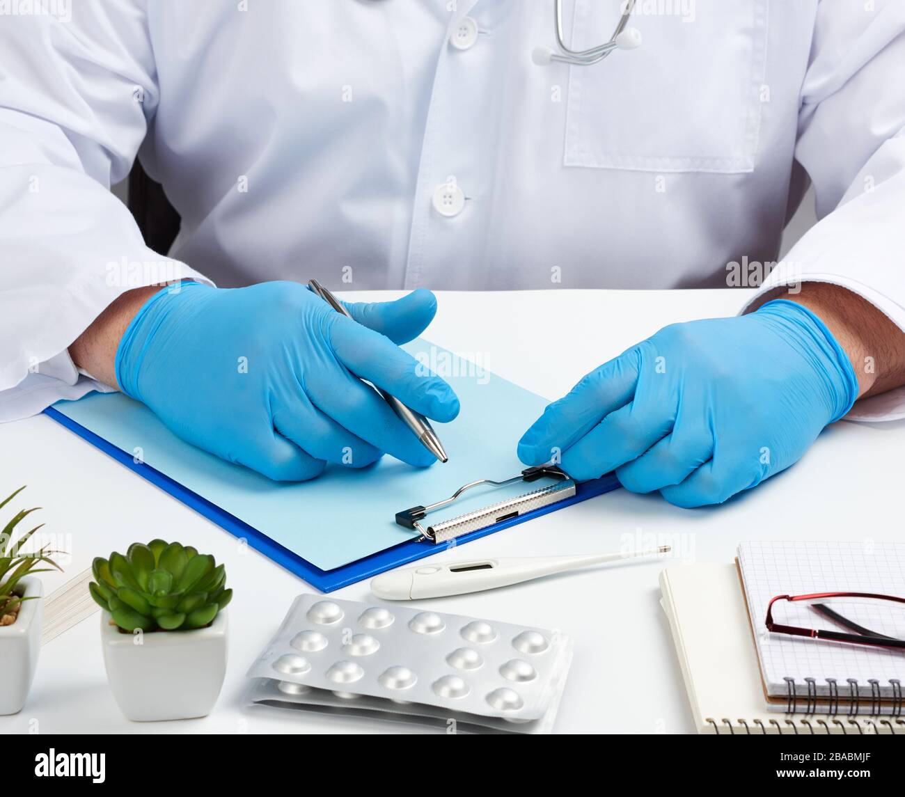 male doctor in a white uniform sits at a white table and writes in a ...