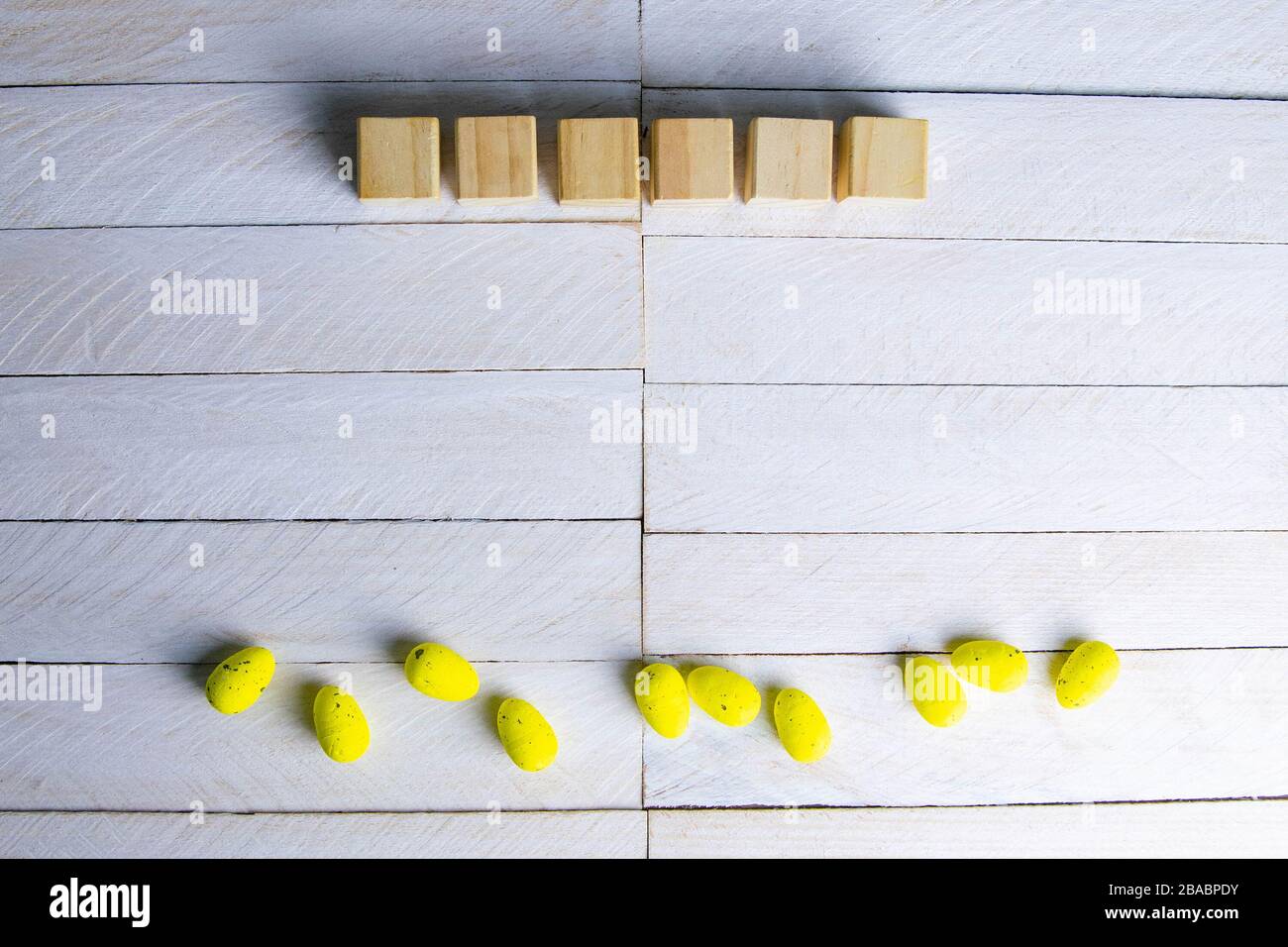 Easter concept. Yellow eggs and wood cubes on a white wooden table ...