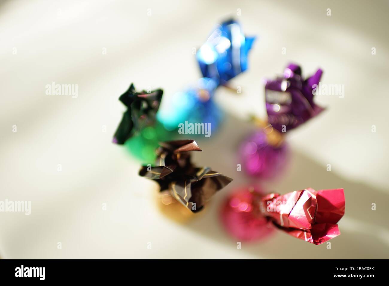 Chocolates in colorful brightly colored wrappers on a sunny table, top ...
