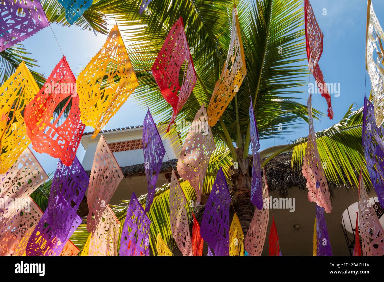 Mexican folk art, papel picado, hanging over a palm lined street in mid ...