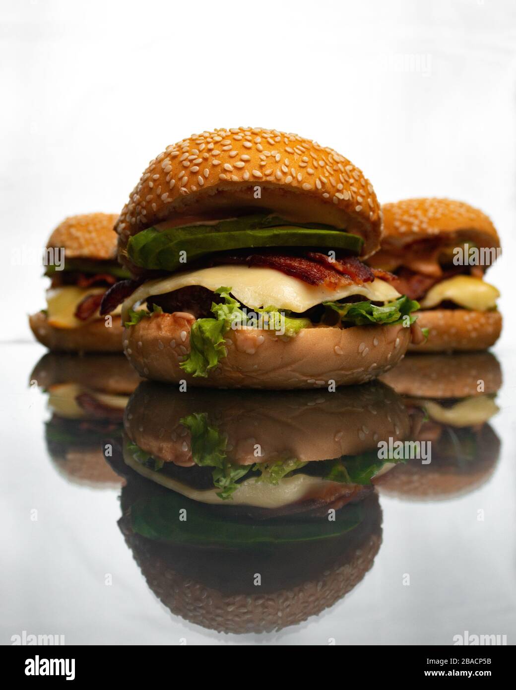 Three delicious burgers with reflections on the ground on a white ...
