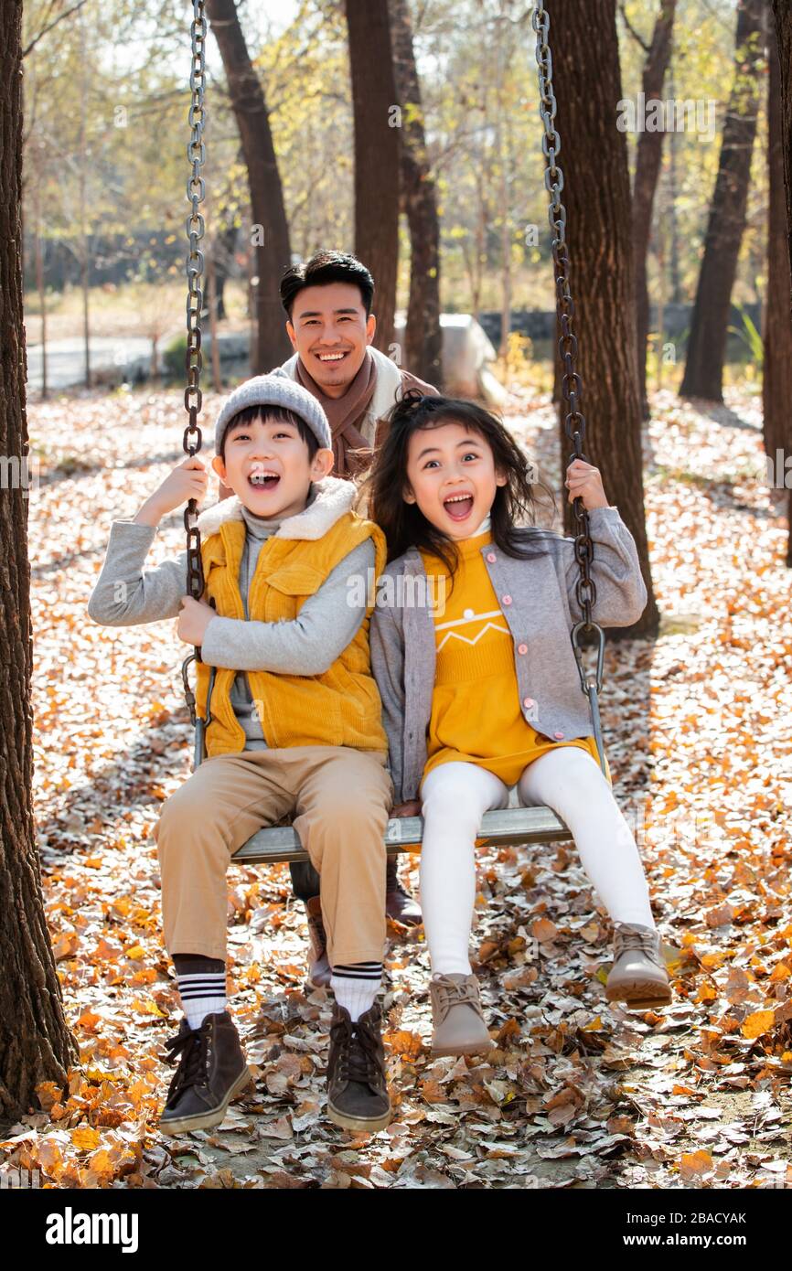 The happy children and father playing on the swings in the outdoor ...