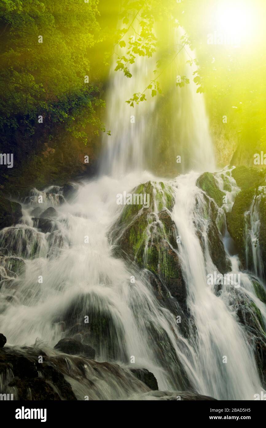 Waterfall in the forest with the moss covered moss lit by the rays of ...