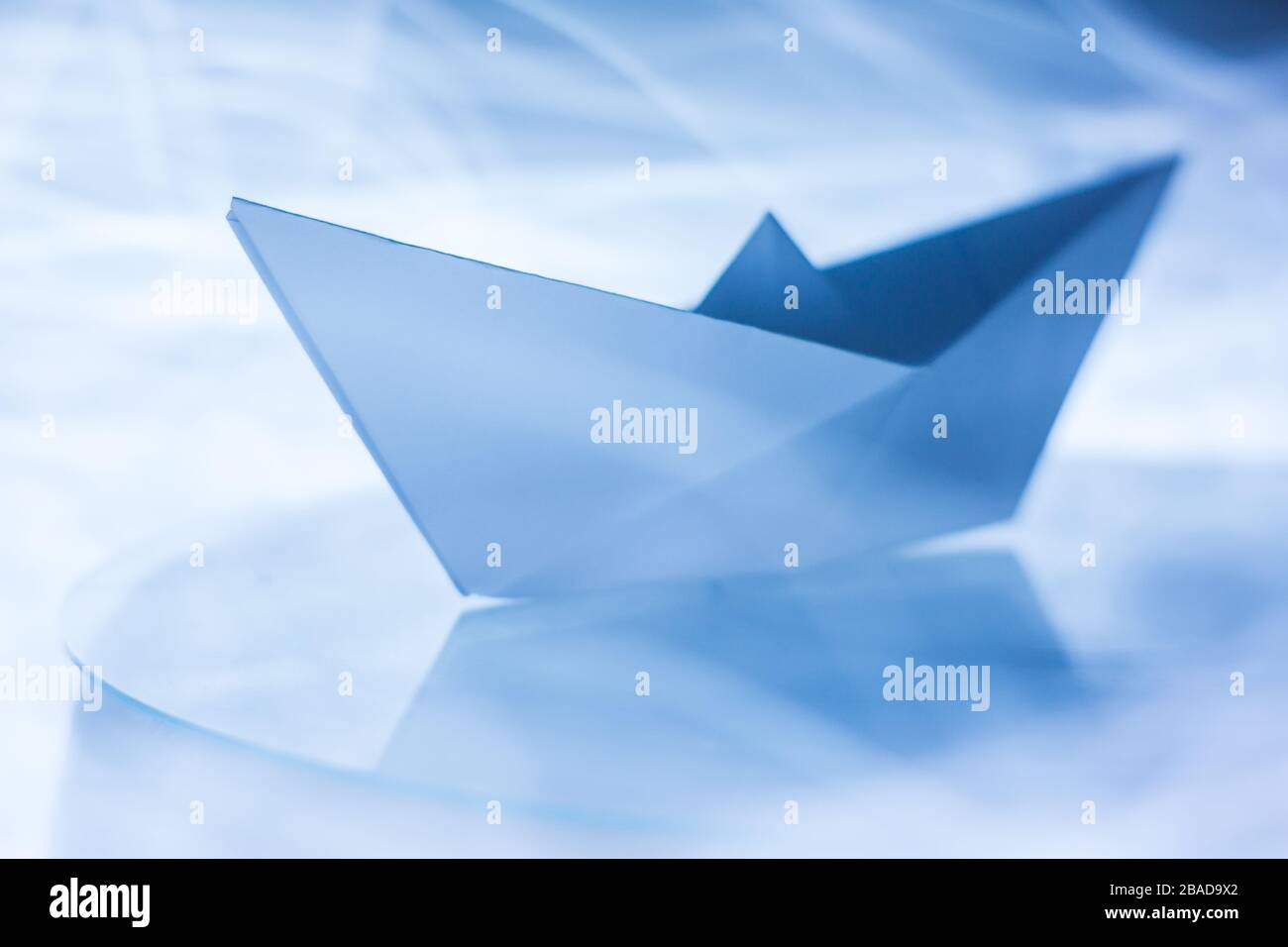 Paper boat splitting blue light trails symbolizing waves in the sea ...