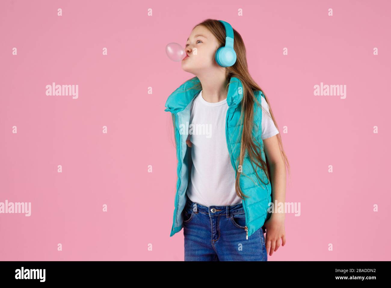 A little girl with headphones explodes pink chewing gum on a pink ...