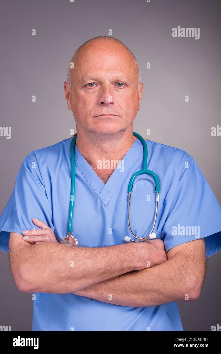 Serious looking doctor with his arms folded, wearing blue scrubs with ...