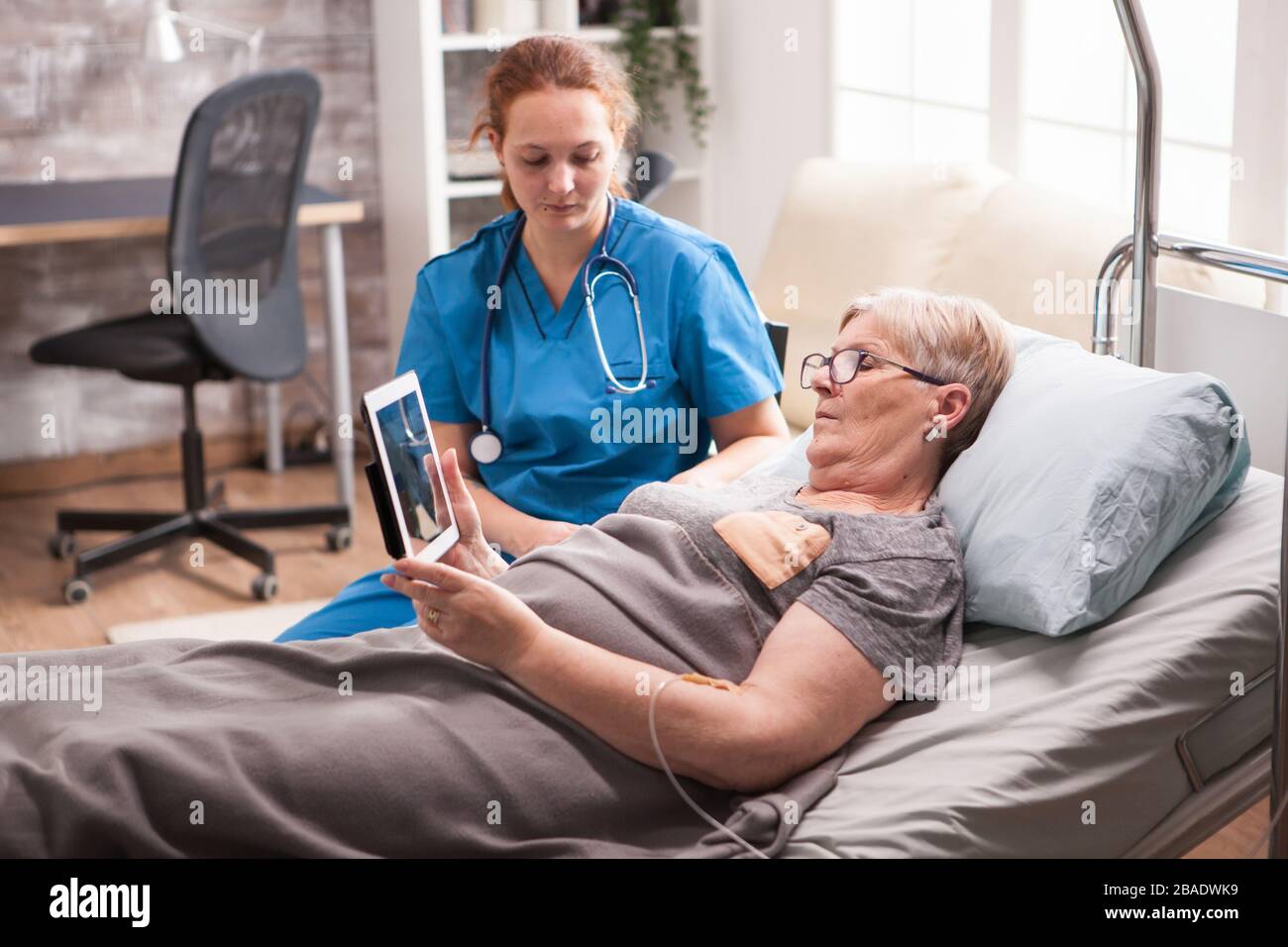 Old woman in nursing home sitting in bed using tablet computer the ...