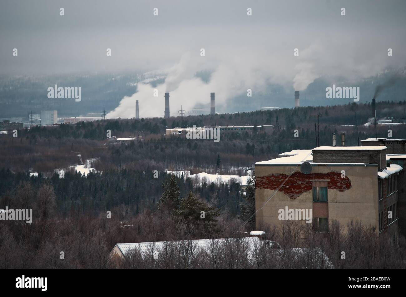 Smoke pipes of a plant over a forest in a post-Soviet city in cloudy ...