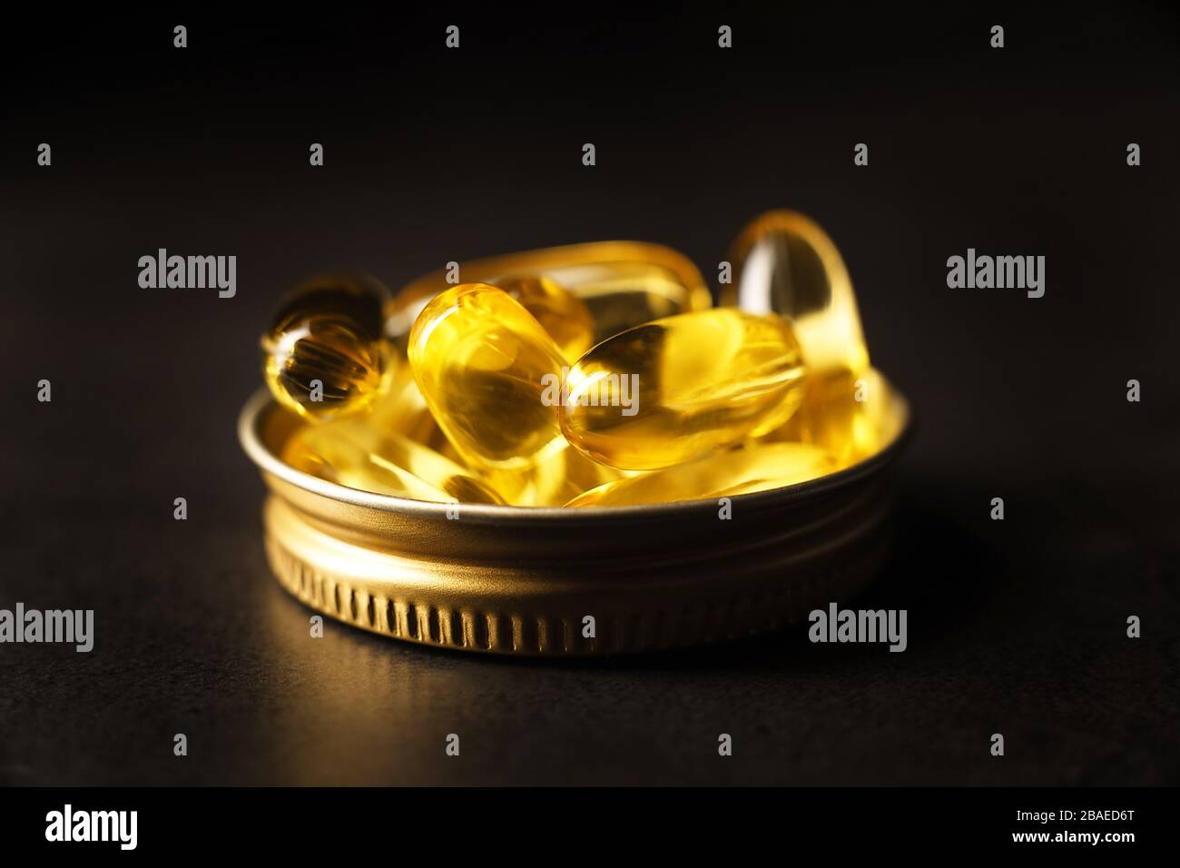 Macro photo of Omega 3 capsules in a golden cap on a black background ...