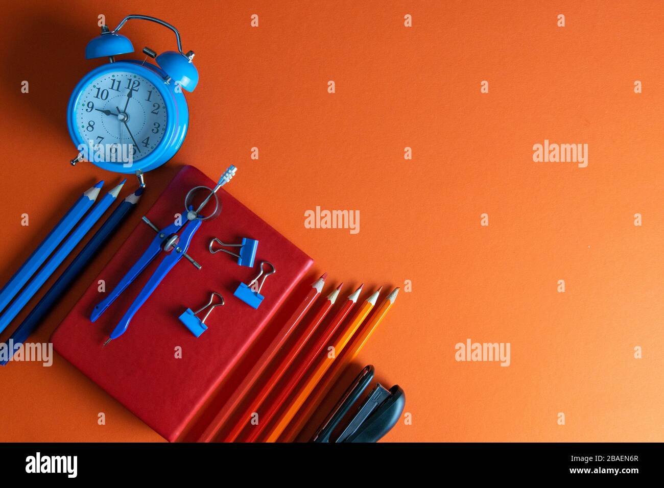 Red notebook with pencils, compass, stapler and clock on an orange ...