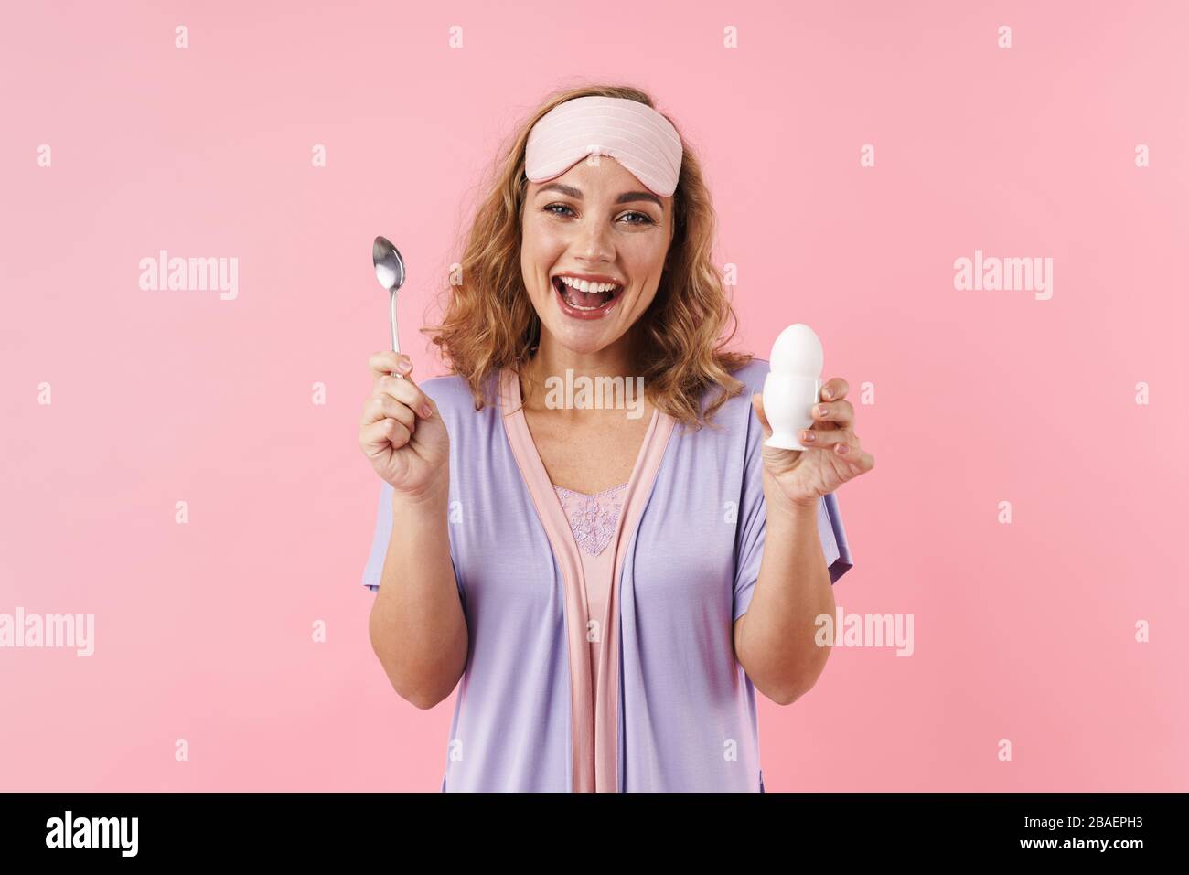 Image of young cheerful woman in sleep mask smiling while holding egg ...