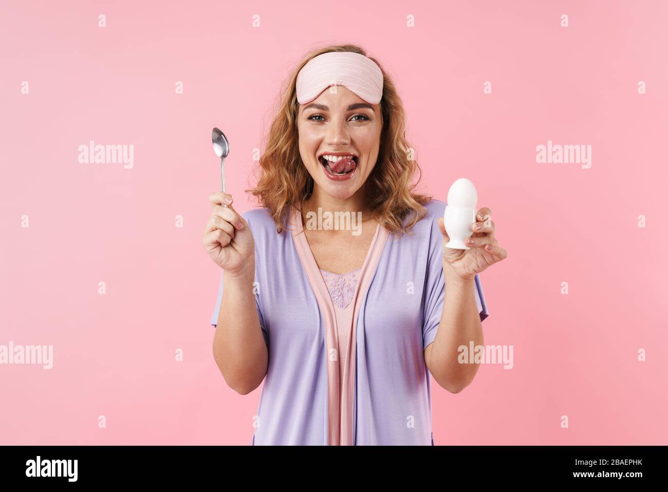 Image of young cheerful woman in sleep mask smiling while holding egg ...