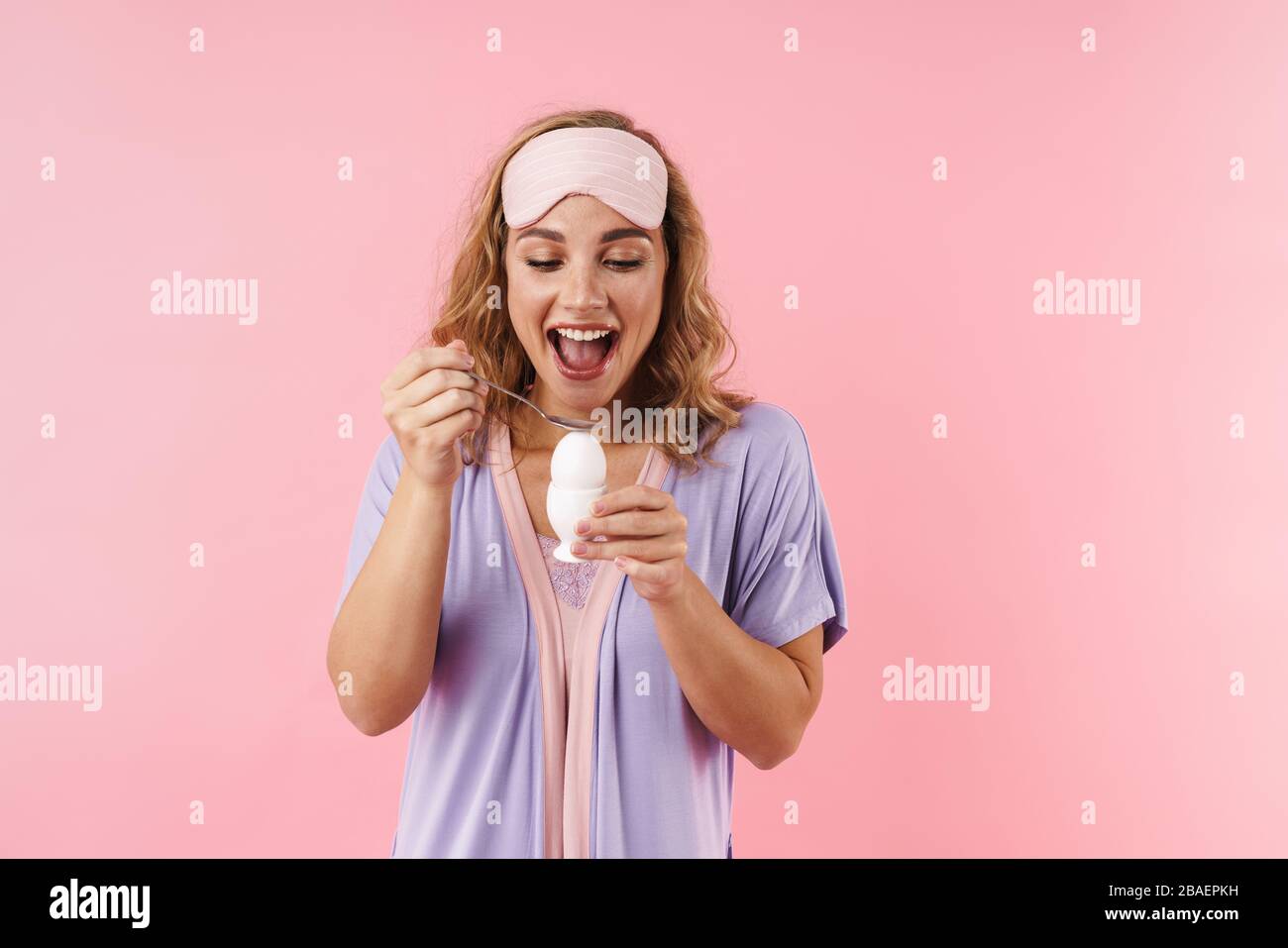 Image of young excited woman in sleep mask smiling while eating egg ...