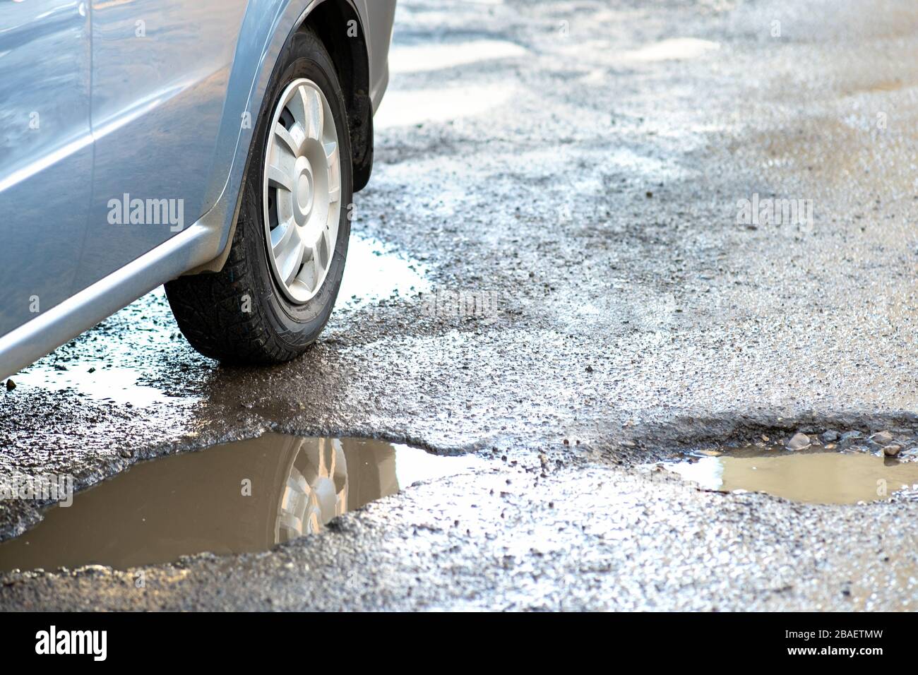 Close up of car wheel on a road in very bad condition with big potholes ...